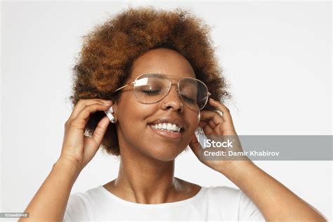 아름 다운 젊은 아프리카계 미국인 여자의 근접 촬영 얼굴만 사진에 고립 된 회색 배경 입고 안경 및 무선 이어폰 기쁘게 미소와 눈 감고 음악을 듣고 무선 인이어 헤드폰에