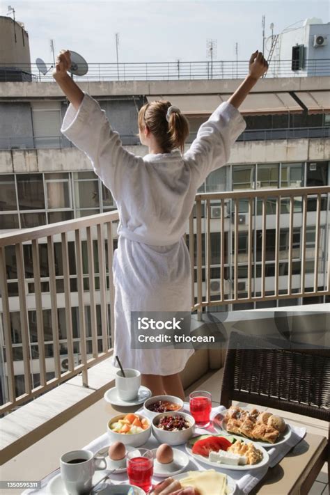 목욕 가운을 입은 젊은 여성이 도시 전망을 감상할 수 있는 발코니에서 아침 식사를 즐기고 있습니다 바쁜 하루 전에 목가적 인