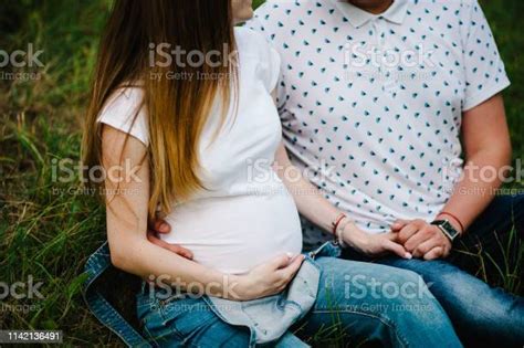 임신 한 소녀와 그녀의 남편은 포옹 손을 잡고 위에 정원 배경에서 야외에서 잔디에 앉아 닫습니다 위쪽 절반 하프 길이 2명에