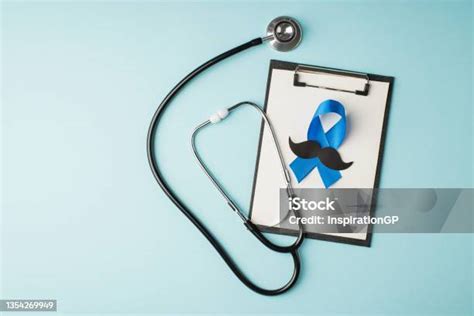 카피스페이스가 있는 고립된 파스텔 블루 배경에 전립선암 인식의 수염 실루엣을 상징하는 청진기 클립보드와 파란 리본의 상단 보기 사진 검사 보기에 대한 스톡 사진 및 기타