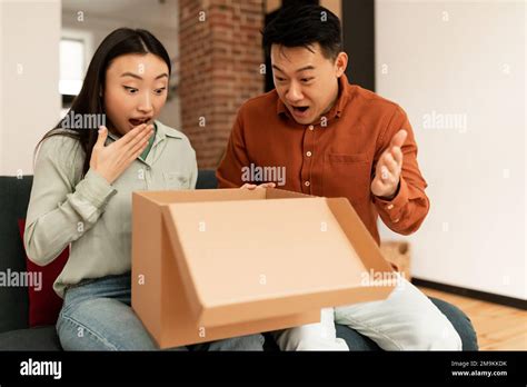 Happy Surprised Asian Couple Unpacking Cardboard Box With Delivered