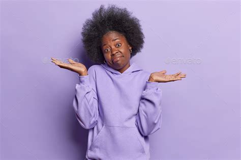 Confused Dark Skinned Young Woman With Bushy Hair Spreads Palms With