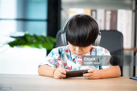 가정용 아이 에서 테이블에 앉아 스마트 폰을 재생 헤드폰과 아시아 태국 소년 사용 전화 및 놀이 게임 4 5세에 대한 스톡 사진