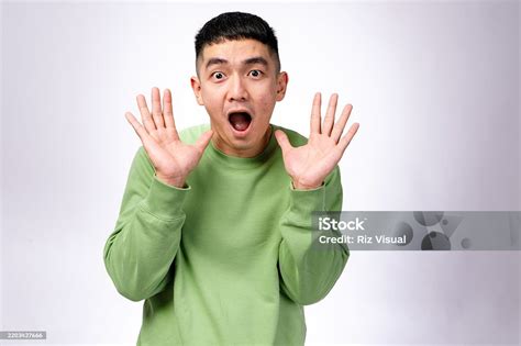 초록색 스웨트셔츠를 입은 흥분한 아시아 남성이 손바닥을 활짝 벌리고 즐거운 표정으로 양손을 들어 올린다 그는 평범한 흰색 배경에 서서 놀라움과 흥분을 전달합니다 30 34