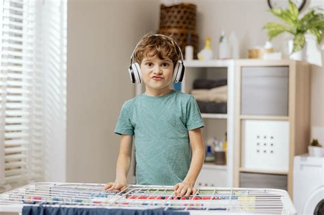 곱슬 머리를 한 소년은 무선 헤드폰을 착용하고 옷 건조기로 서서 어린이 놀이 바보 세탁실에서 집안일을하면서 음악을 듣습니다 개념에 대한 스톡 사진 및 기타 이미지 Istock