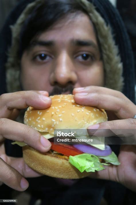 얼굴을 보여주는 앞에서 손에 햄버거를 들고 인도 남자의 이미지 먹고 건강한 수제 치즈 버거 햄버거 햄버거 빵에 참깨 녹은 치즈 토마토 붉은 양파 슬라이스와 양상추 갈색 빵에