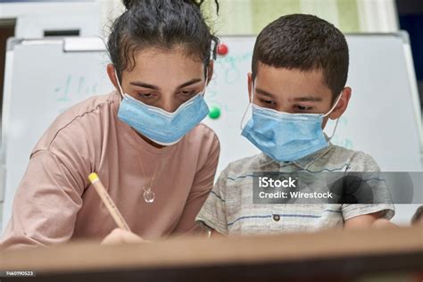 학교에서 수업 중에 어린 학생이 그림을 그리도록 돕는 안면 마스크를 쓴 젊은 여성 미술 교사 2명에 대한 스톡 사진 및 기타
