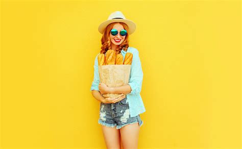 초상화 행복 한 웃는 여자 긴 흰 빵 바게트와 종이 가방을 들고 밀 짚 모자를 입고 화려한 노란색 배경에 반바지 가방에 대한 스톡 사진 및 기타 이미지 Istock