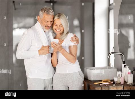 Happy Senior Couple Checking Smartphone Together In Bathroom During
