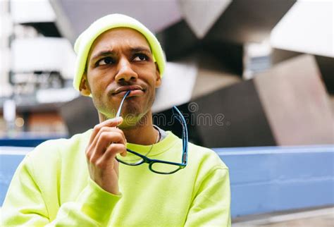 Pensive Multiracial Man Biting Glasses While Standing In City Stock