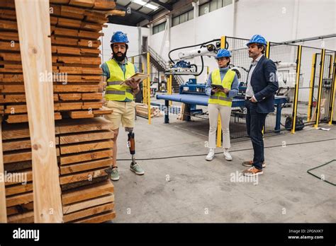 Engineer Explaining By Stack Of Planks With Colleagues In Factory Stock
