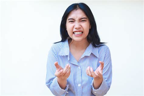 화난 아시아 여자가 파란색 줄무늬 셔츠를 입고 비명을 지르고 흰색 배경에 고립되어 서서 카메라를 보면서 손을 쪼갠다 20 24