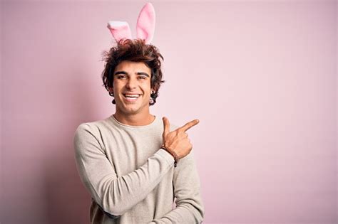 고립된 분홍색 배경 위에 서있는 부활절 토끼 귀를 들고있는 젊은 잘생긴 남자는 얼굴에 행복하고 자연스러운 표정으로 손과
