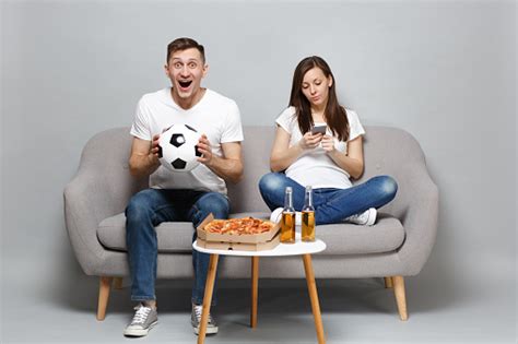 커플 흥분 남자 축구 팬 응원 축구 공 회색 배경에 고립 된 휴대 전화를 사용 하 여 지루한 여자와 함께 좋아하는 팀 지원 사람들의 감정 스포츠 가족 레저 라이프 스타일