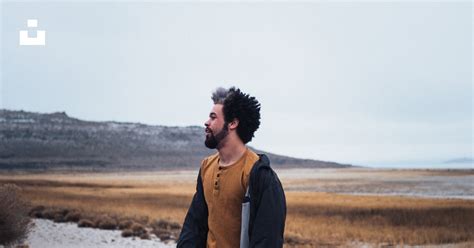 Man In Brown Jacket And Black Pants Standing On Gray Sand During