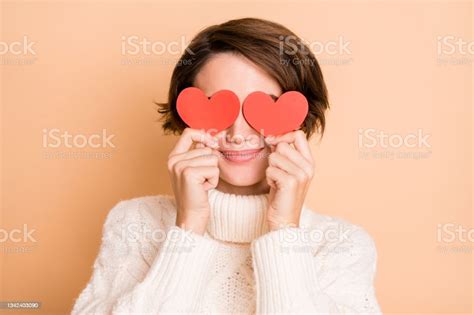 파스텔 베이지 색 배경에 고립 된 하트 모양의 카드 뒤에 눈길을 숨기는 여학생의 사진 초상화 하트 모양에 대한 스톡 사진 및