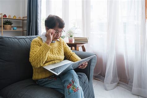 소파에 앉아 행복한 얼굴로 거실에서 노트북 랩탑 컴퓨터를 사용하는 고위 아시아 여성 65 69세에 대한 스톡 사진 및 기타