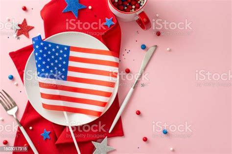 미국 독립 기념일 파티를 위한 축제 메뉴 접시 깃대 포크 나이프 스프링클이 있는 머그잔 냅킨 파스텔 핑크 배경의 반짝이는 별이 있는 탑 뷰 테이블 설정 0명에 대한 스톡