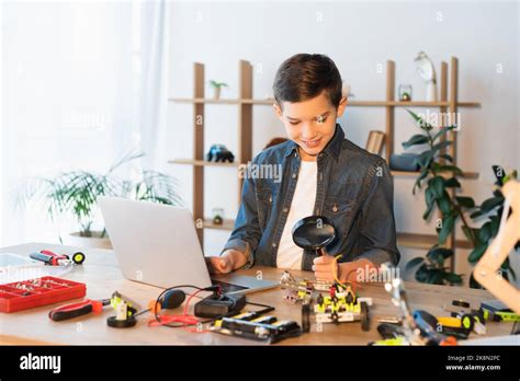 Smiling Boy Holding Magnifying Glass Near Parts Of Robotics Model And
