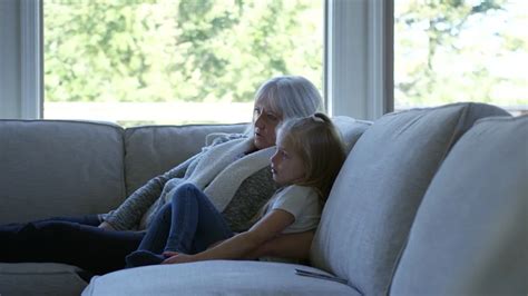 Grandmother And Granddaughter Watch Television On The Couch Together