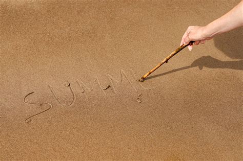 해변의 젖은 모래에 글을 쓰는 중년 여성 여름이라는 단어를 긁는 나무 막대기가있는 인간의 손 40 49세에 대한 스톡 사진 및