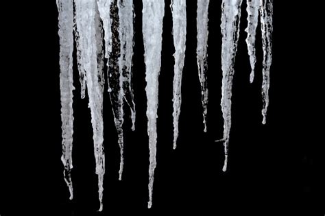 봄에는 길이와 너비가 다른 투명한 Icicles가 지붕에서 매달려 있습니다 클로즈업 질감이있는 검은 색 배경 고드름에 대한 스톡