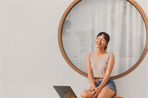 젊은 매력적인 아시아 프리랜서 여성은 여름 방학 동안 노트북 컴퓨터로 일하는 창문 집 앞 벤치에 앉아 있습니다 행복한 아시아