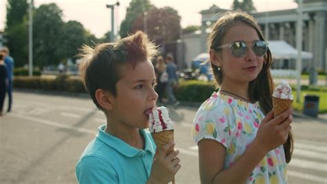 Linda hermana y hermano comiendo helado niños sonrientes caminando en el parque de diversiones