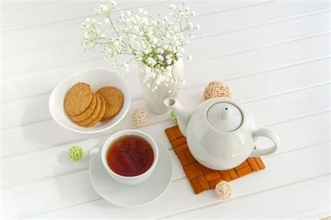 흰색 세라믹 컵과 찻주전자 흰색 나무 테이블 배경에 꽃과 쿠키가있는 흰색 꽃병 상단보기의 부드러운 빛 이미지 아침 식사와 차에
