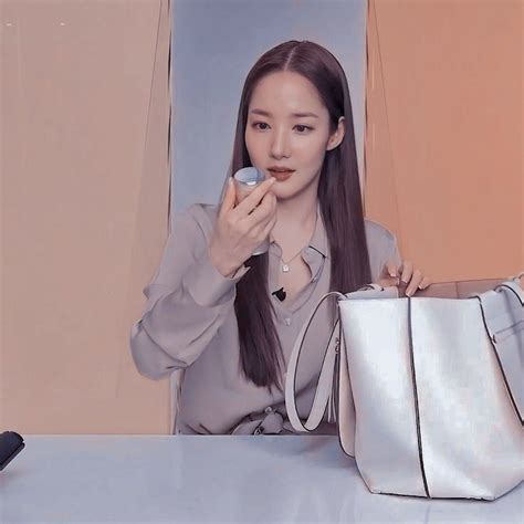 A Woman Holding A Cell Phone Next To A White Purse On Top Of A Table