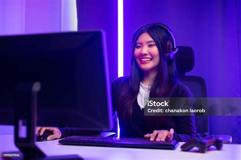 프로 게이머 거실에 컴퓨터 Pc가있는 의자에 앉아있는 젊은 아시아 예쁜 여자 행복한 여성 전문 스트리머 중국어 착용 헤드폰