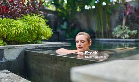 발리에서 열대 휴가 기간 동안 고급스러운 호텔의 햇볕이 잘 드는 무성한 돌 수영장에서 야외에서 휴식을 취하는 아름다운 평화로운 여성 앞마당 또는 뒷마당에 대한 스톡 사진 및