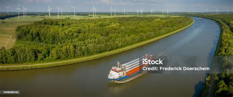 풍력 터빈 블레이드를 실은 화물선이 풍력 발전 단지를 배경으로 킬 운하를 항해하고 있습니다 화물선의 풍력 터빈용 블레이드 운송 지속 가능한 자원에 대한 스톡 사진 및 기타