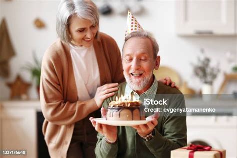 생일 축하 기간 동안 불이 켜진 촛불로 초콜릿 케이크를 들고 파티 모자를 쓴 행복한 노인 주기에 대한 스톡 사진 및 기타 이미지