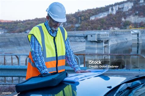 파란색과 흰색 체크 무늬 셔츠를 입고 댐 옹벽 앞에서 주황색과 노란색 반사 안전 조끼를 입은 수염과 안경을 쓴 엔지니어 50 54세에 대한 스톡 사진 및 기타 이미지