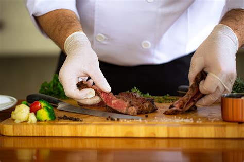 요리사가 도마에 고기를 자르고 검은 제복을 입은 전문 요리사가 나무 다진 판에 생 스테이크를 소금으로 칠하는 모습 짙은 파란색