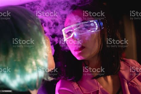 Female Portrait Of Two Women Who Wear Futuristic Glasses And Using Vape