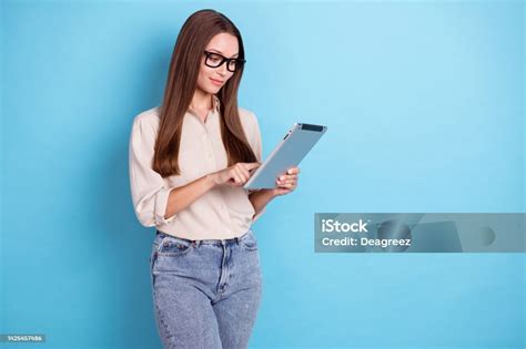 베이지 색 블라우스 청바지를 입은 귀여운 꽤 사랑스러운 소녀의 초상화는 파란색 배경에 고립 된 태블릿의 그래픽 통계를 봅니다