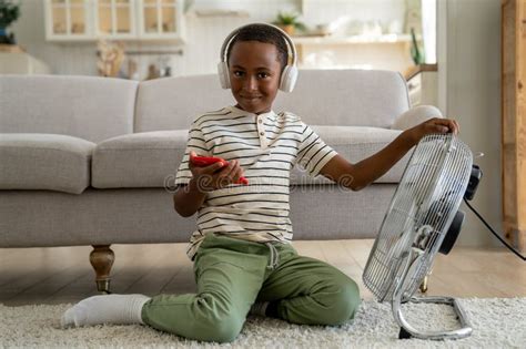Niño Sonriente Sentado En El Suelo Enfriándose Con El Ventilador Eléctrico Escuchar Música En El