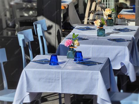 Premium Photo Line Of Cute Square Tables With Patterned Blue And White Tablecloths And Flowers