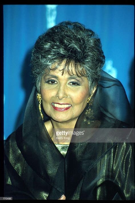 An Older Woman Wearing A Black Jacket And Gold Earrings