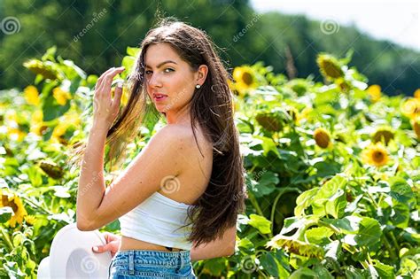 Beautiful Woman Posing In A Field Of Sunflowers In A White Top And Hat