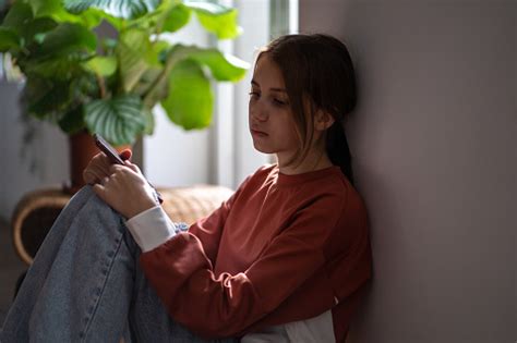 핸드폰을 들고 불안한 십대 사춘기 소녀가 바닥에 앉아 전화를 기다린다 도움이 필요하다고 느낀다 슬픔에 대한 스톡 사진 및 기타