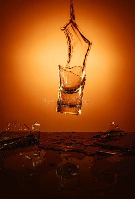 Exploding Glass Cup With Water Shattering Over Orange Background Stock