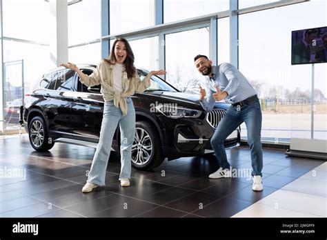 Man And Woman Inspecting A New Car Before Buying In A Car Dealership