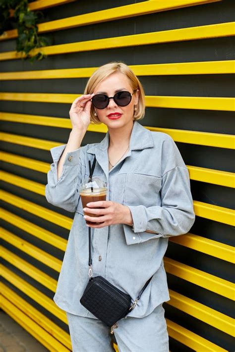 Stylish Young Blonde In Sunglasses Walks Around The City And Drinks A