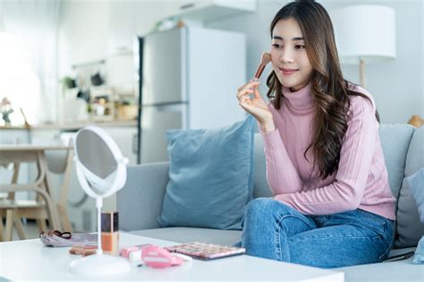 아시아 의 전문 여성 아티스트는 메이크업을 즐기며 집에 머물러 있습니다 젊은 매력적인 아름다운 소녀는 소파에 앉아 거울과 얼굴에