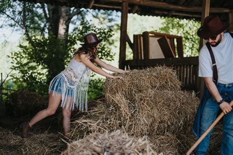 Young Couple Working Together In A Barn Stacking Hay Bales On A Rustic