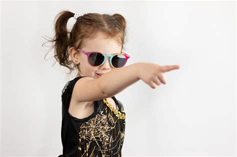 두 개의 포니 테일과 선글라스에 검은 색과 금색 드레스를 입은 어린 쾌활한 소녀 검지 손가락으로 가리키는 슬픈 아이의 흰색