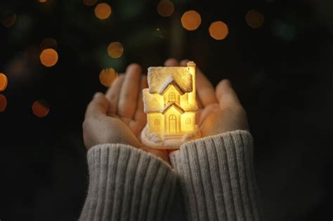 Manos Sosteniendo Casita Iluminada En Las Luces Del árbol De Navidad